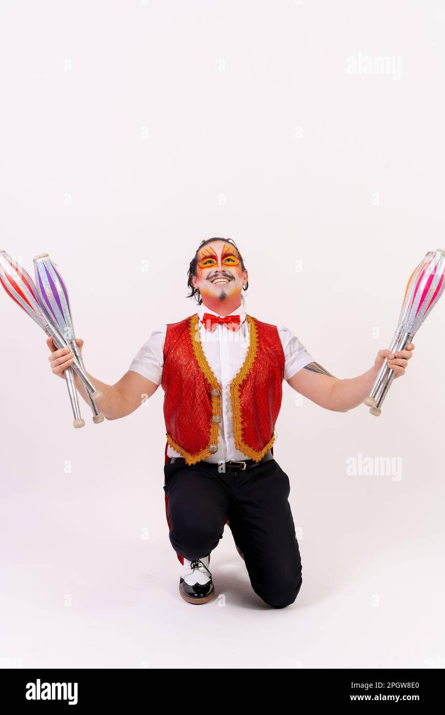 A cheerful circus performer skillfully juggling a number of clubs ...