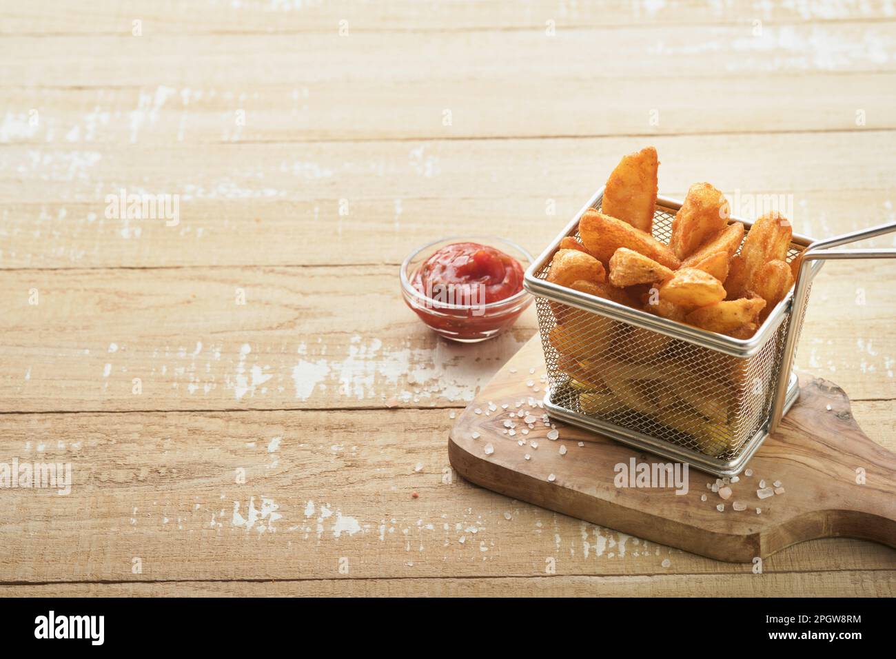 French fries in metal wire basket with salt and ketchup on old wooden ...