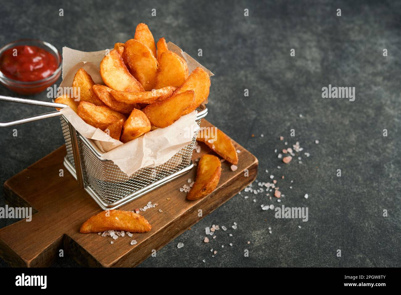 French fries in metal wire basket with salt and ketchup on old wooden ...