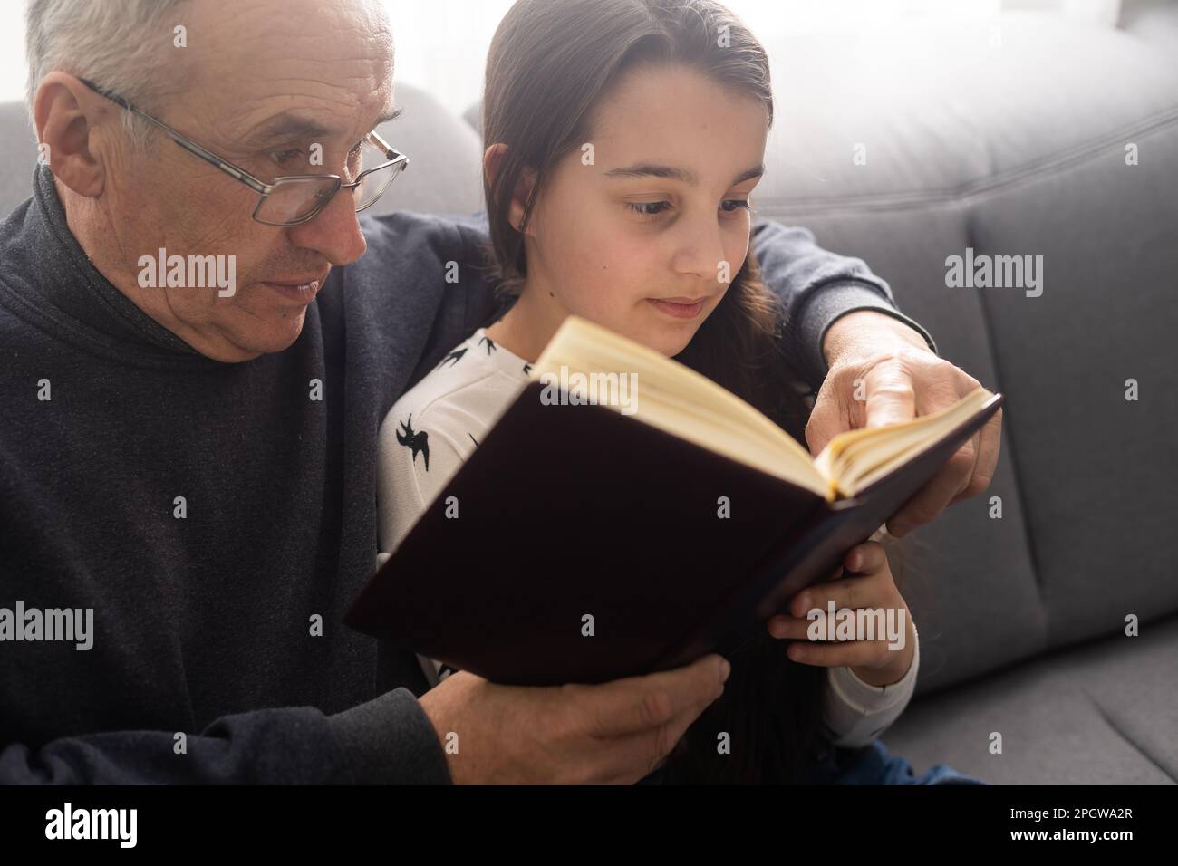 Photo of aged old grandpa little pretty granddaughter sit sofa hugging ...