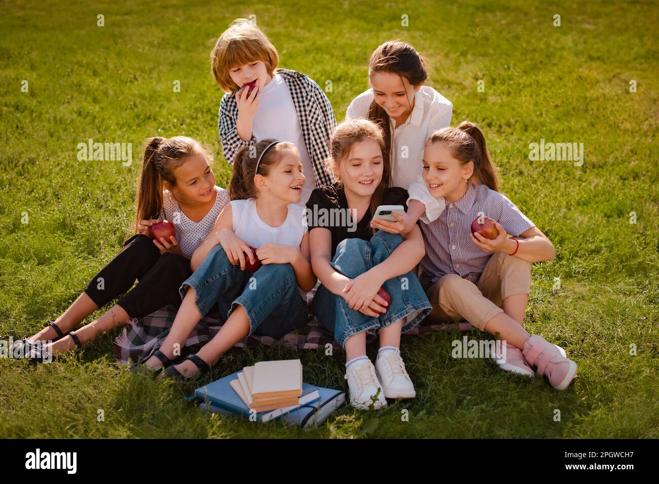 Happy children sitting on green grass and watch video on mobile phone ...