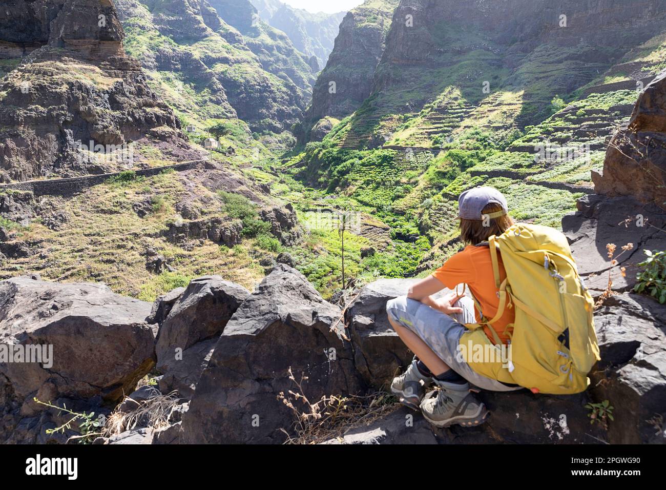 Boy sitting on rocks looking at the green valley while hiking on a most ...