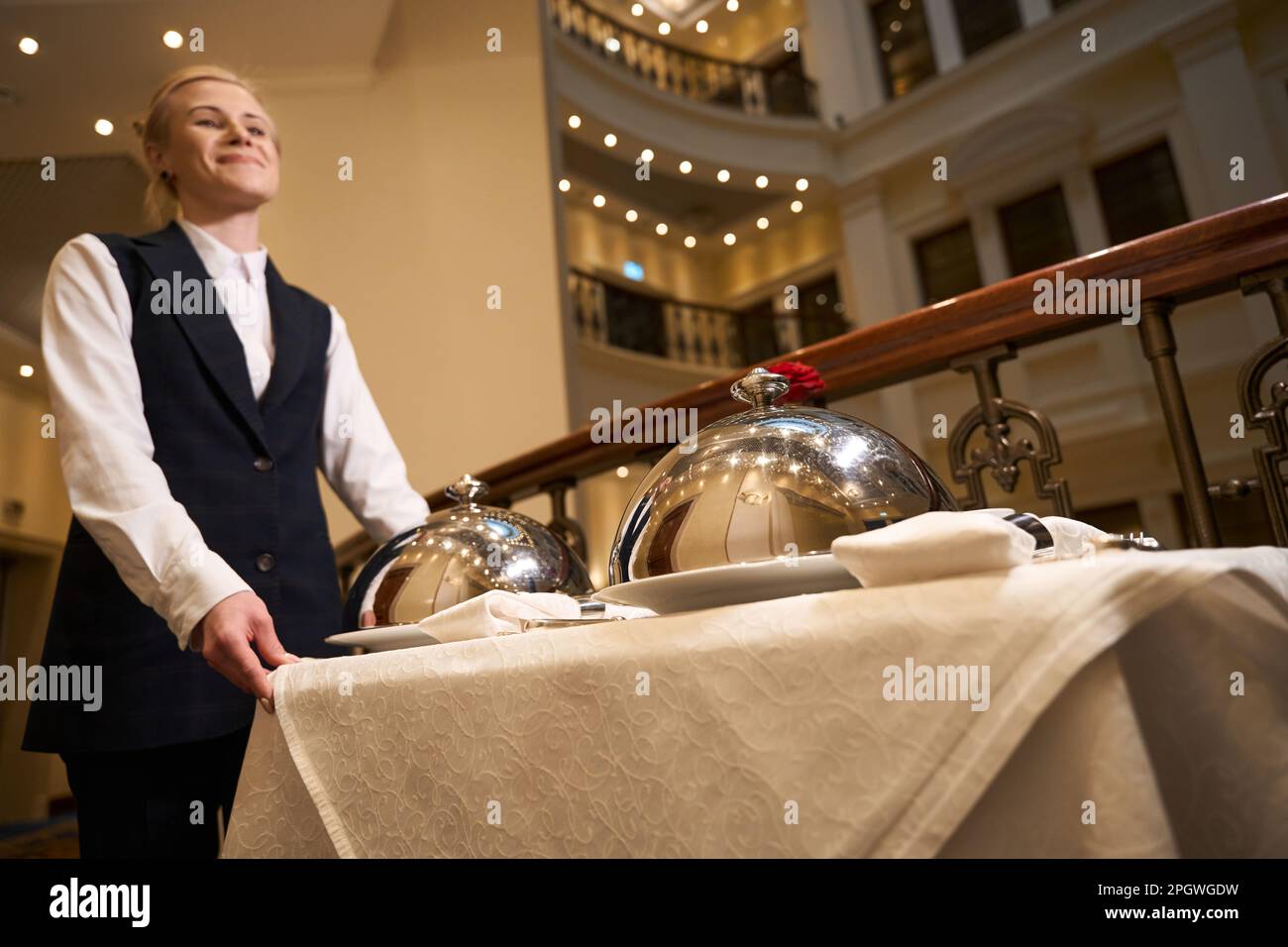 Joyful waitress carries serving cart along corridor of chic hotel Stock ...