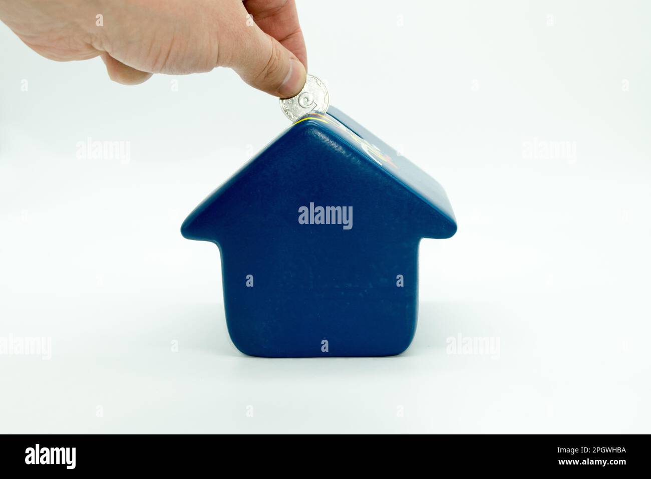View of a hand throwing a coin into a navy blue piggy bank house on a ...