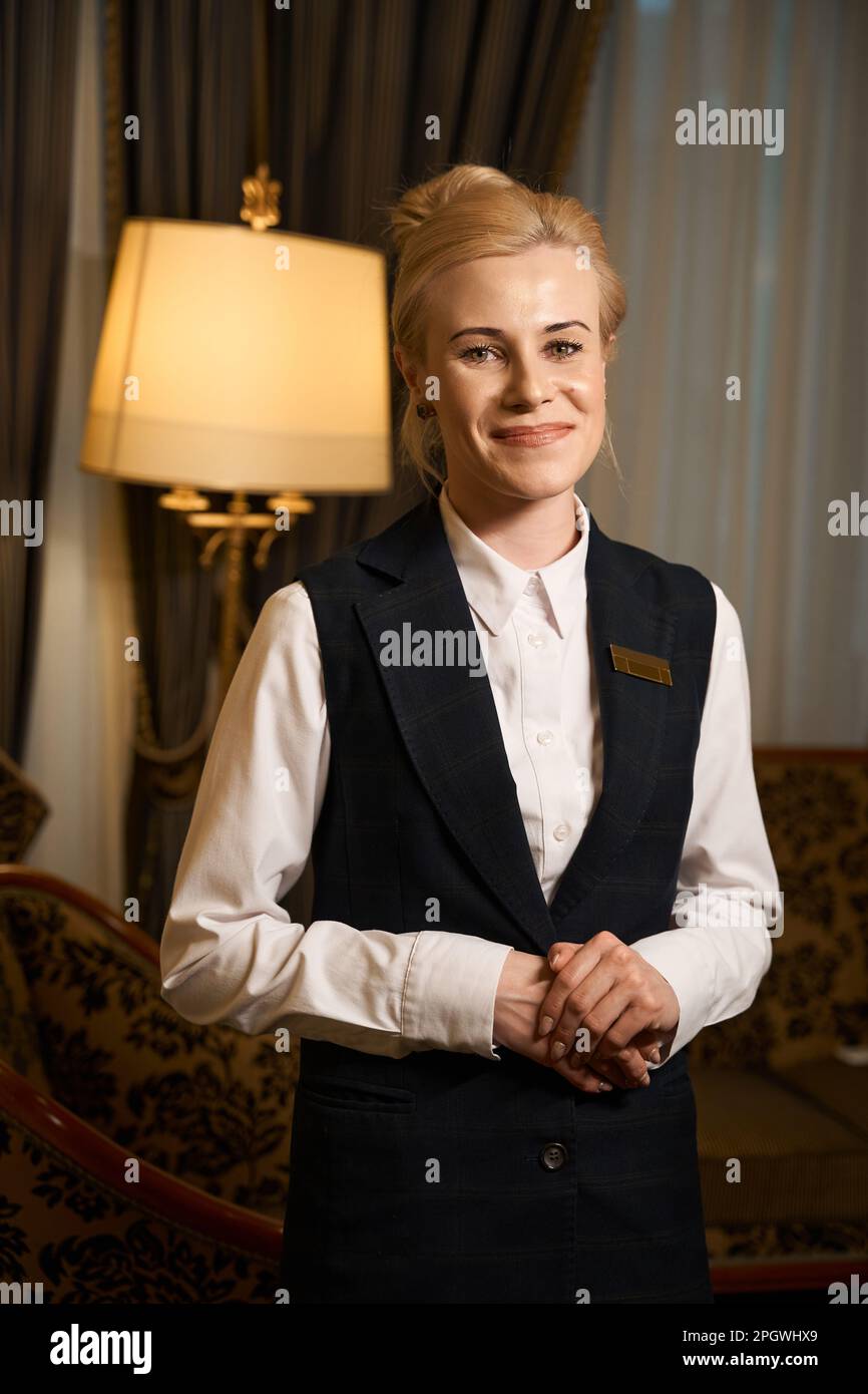 Pretty female hotel manager stands in room with luxurious interior ...