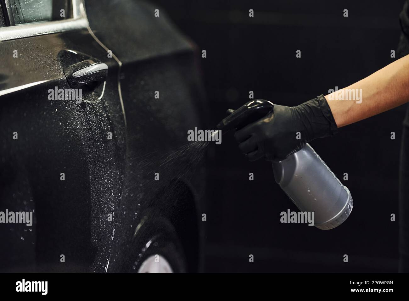 Spraying the vehicle. Modern black automobile get cleaned by woman ...