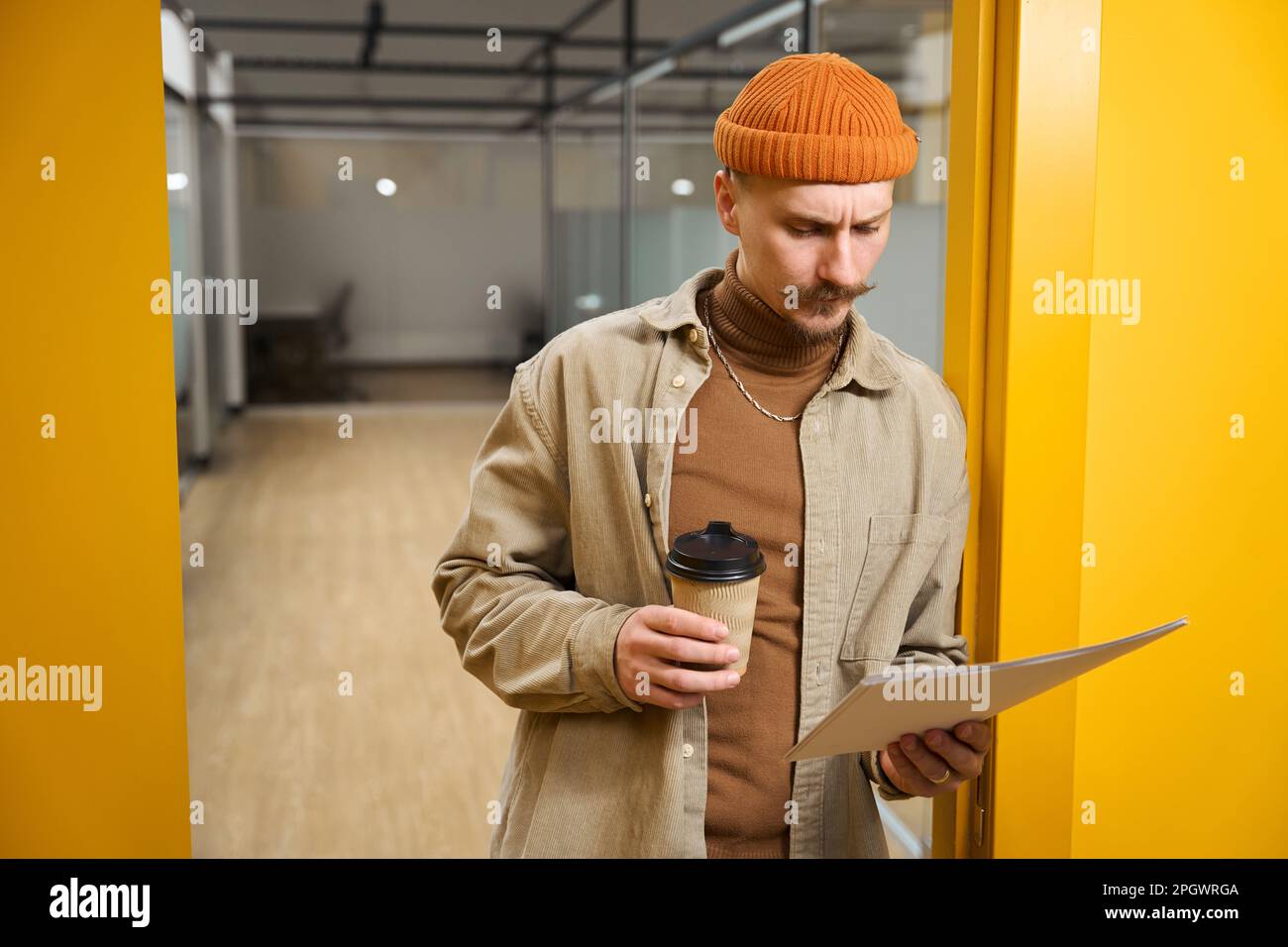 Focused young office worker dealing with paperwork during coffee break ...