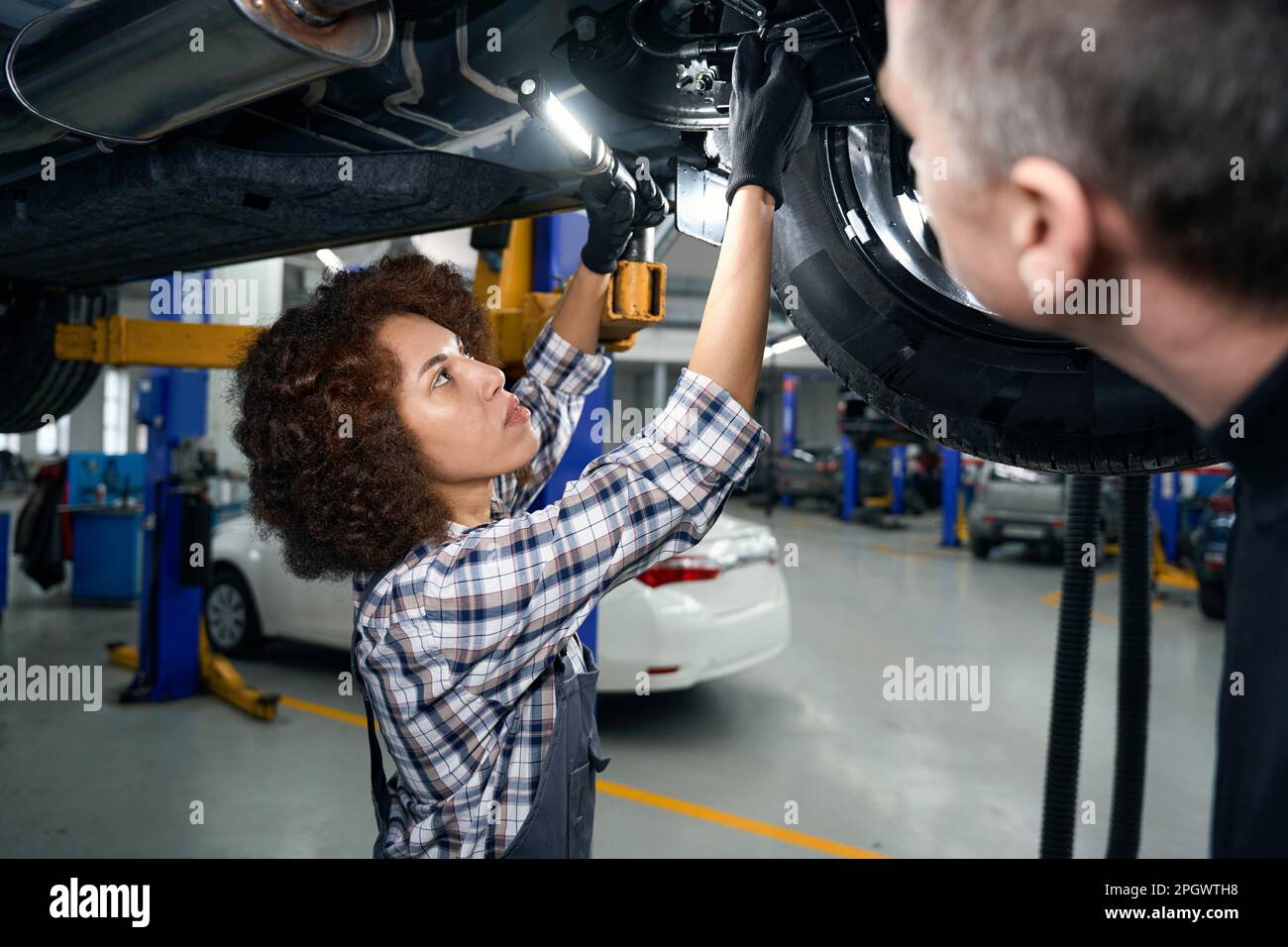 Multiracial female auto mechanic in overalls and client inspecting car ...