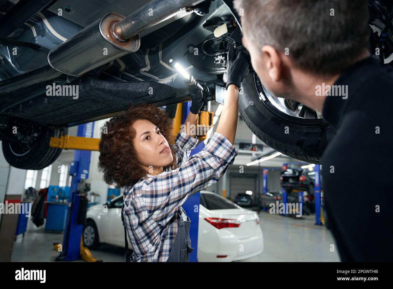 Woman auto mechanic and a client inspect car from below Stock Photo - Alamy