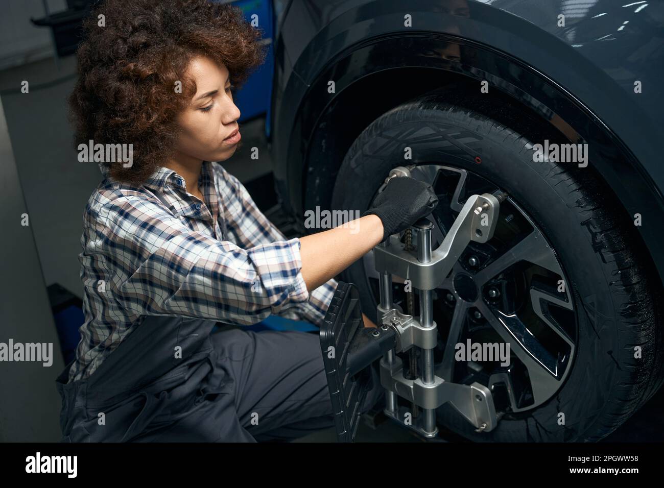 Woman auto mechanic performs wheel balancing, adjusts wheel alignment ...