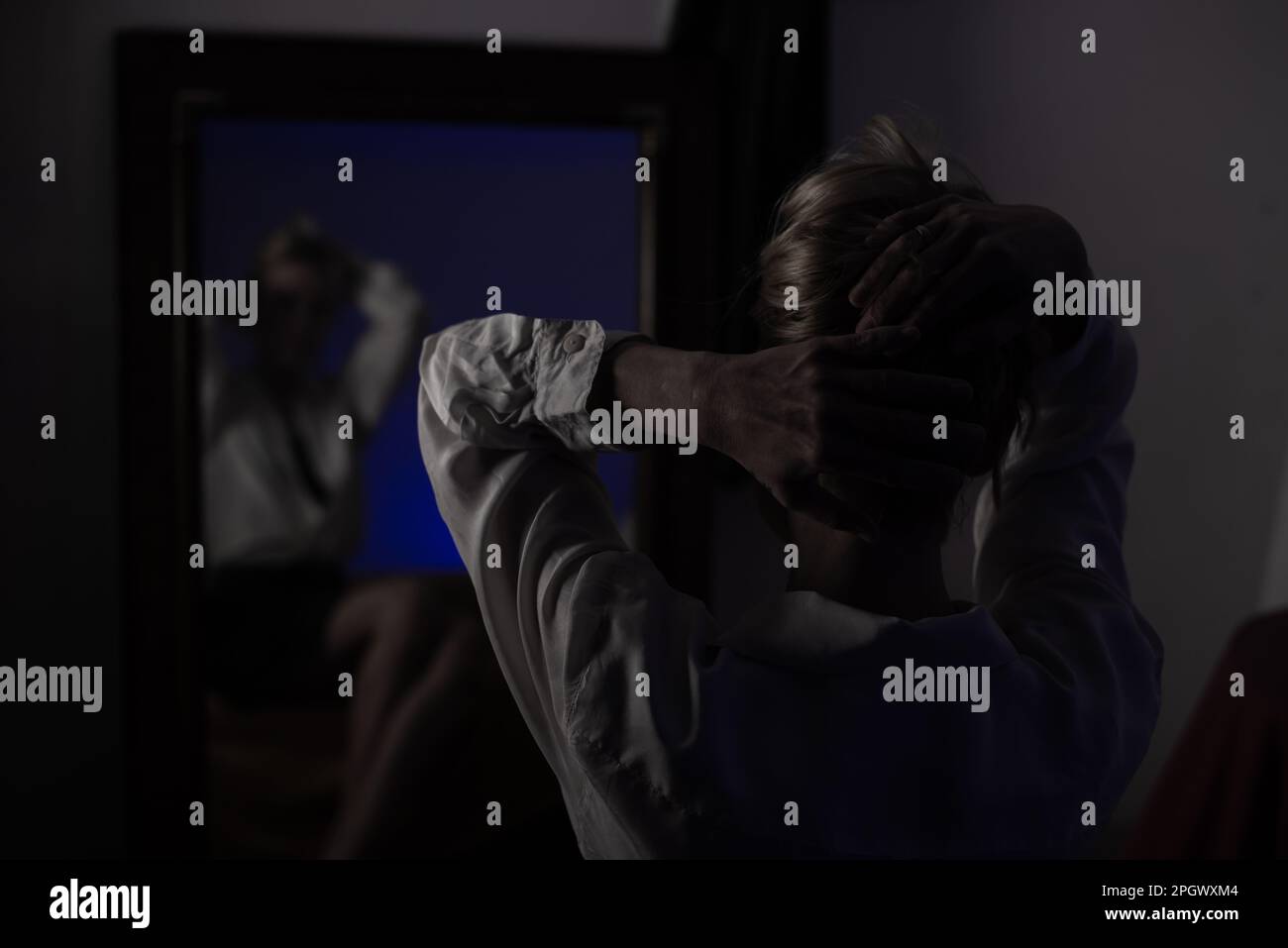 Unrecognizable woman in reflection in front of a mirror in a dark room ...