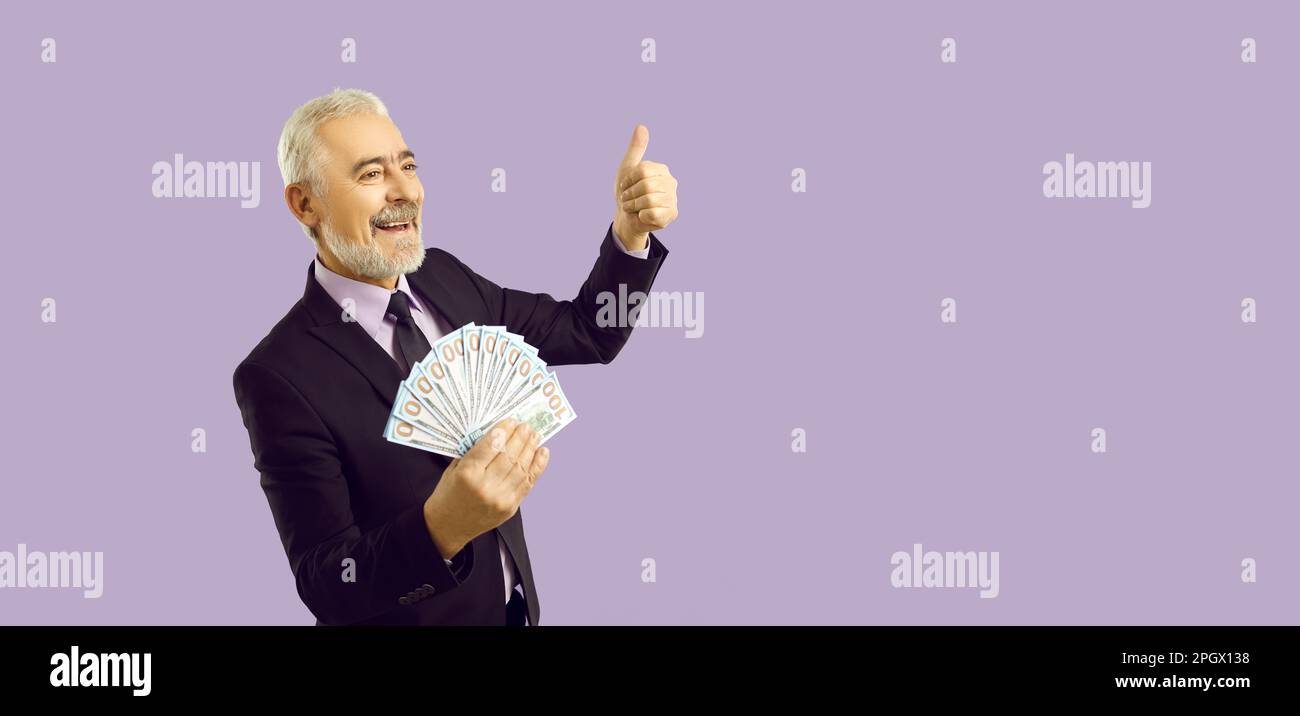 Rich old man holding money and giving thumbs up isolated on copy space ...