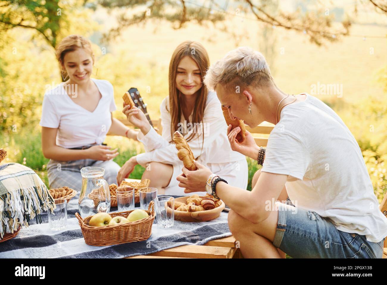 Sitting by picnic table. Group of young people have vacation outdoors ...