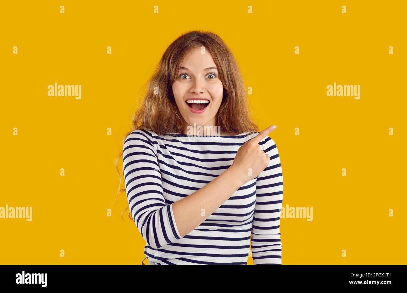 Young laughing excited woman with wavy hair is pointing on copy space ...