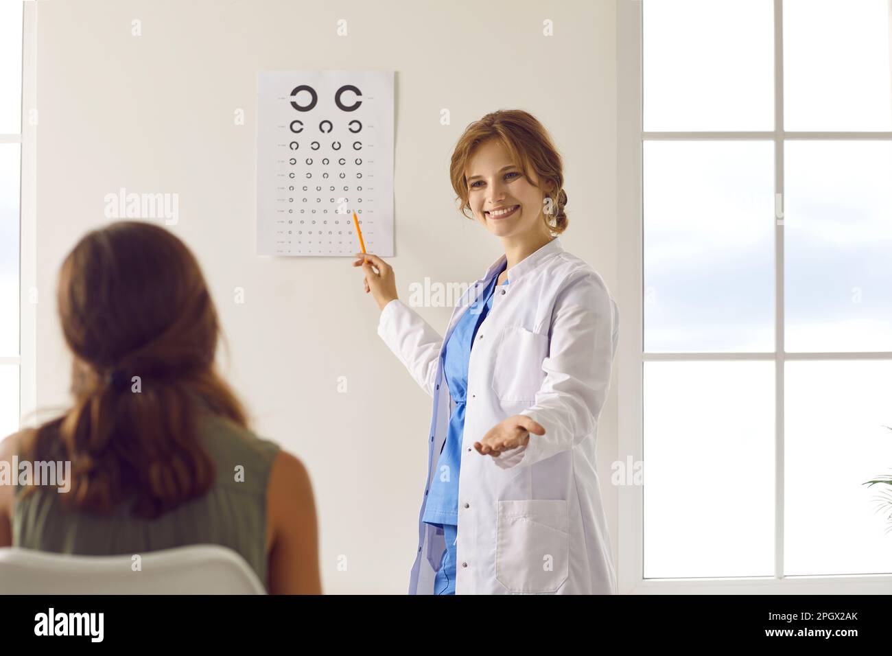 Happy Caucasian female optician in white medical uniform tests vision ...