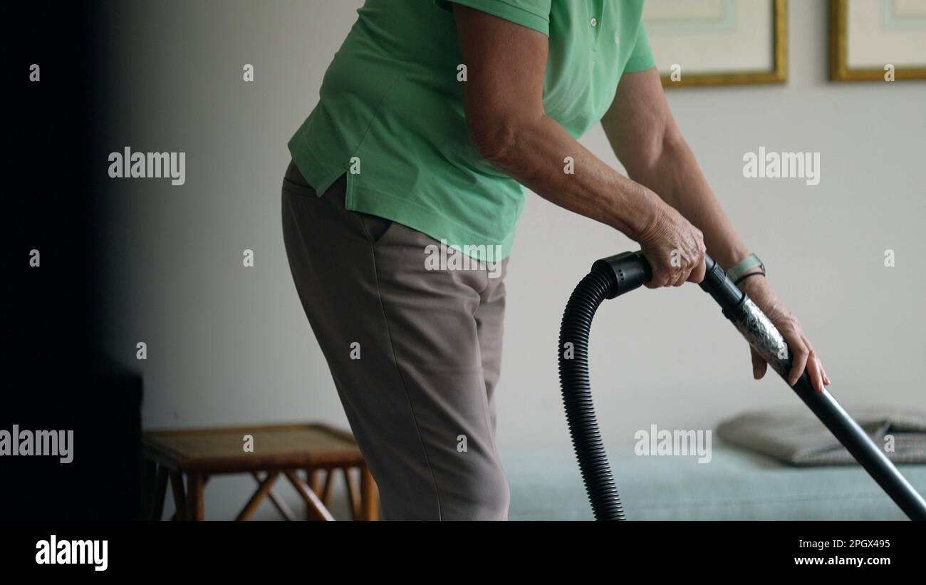 Senior woman vacuuming room. Older person cleaning household doing ...