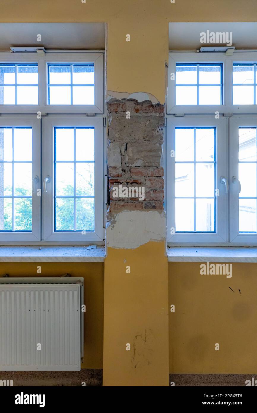 A pillar with peeling plaster between two windows inside an old ...