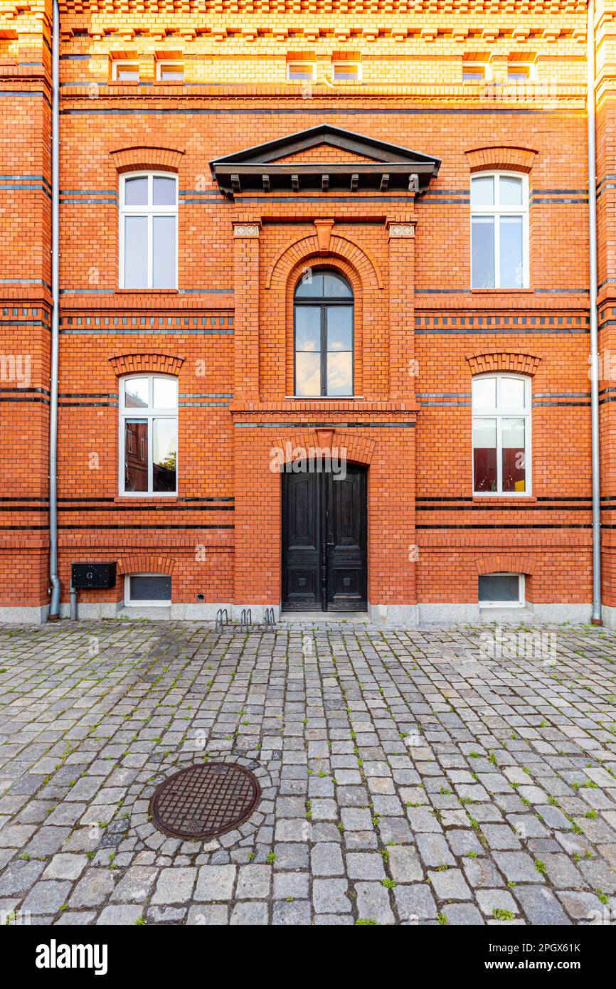 The front of a renovated tall brick building with large black doors ...