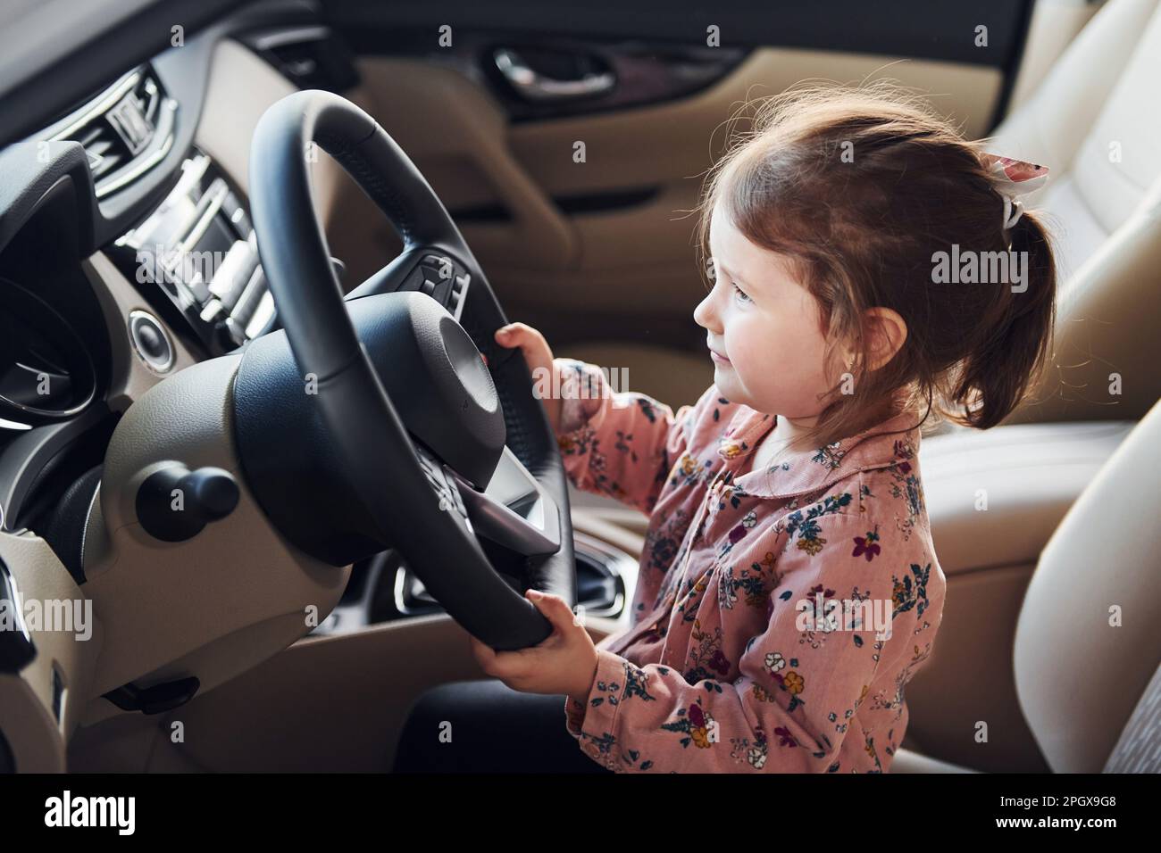 Cute little girl sitting on the driver's seat inside of modern car ...