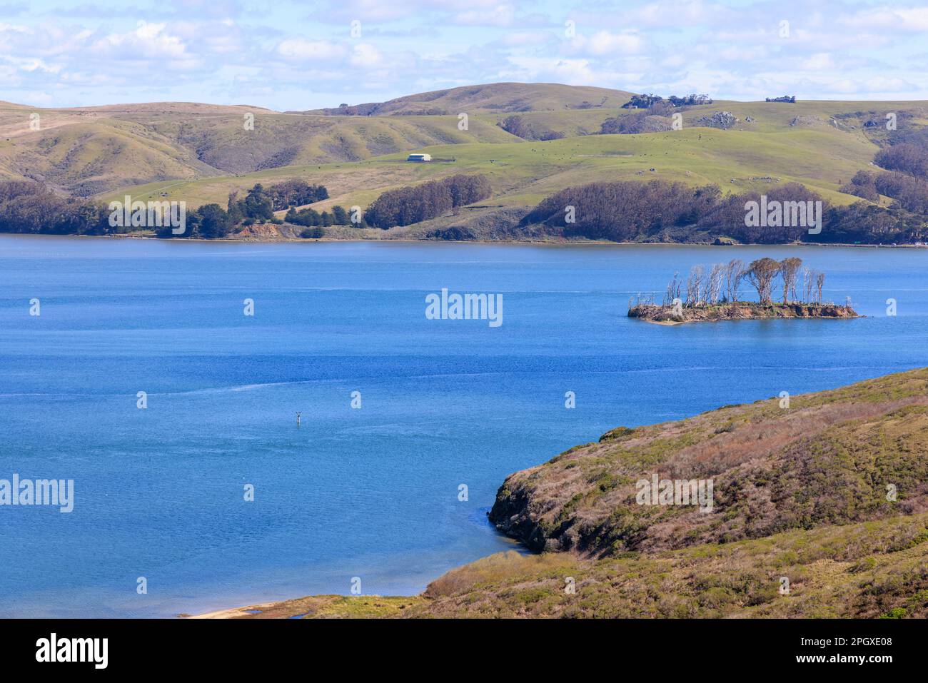 Small island in blue waters and rolling green hills on California coast ...