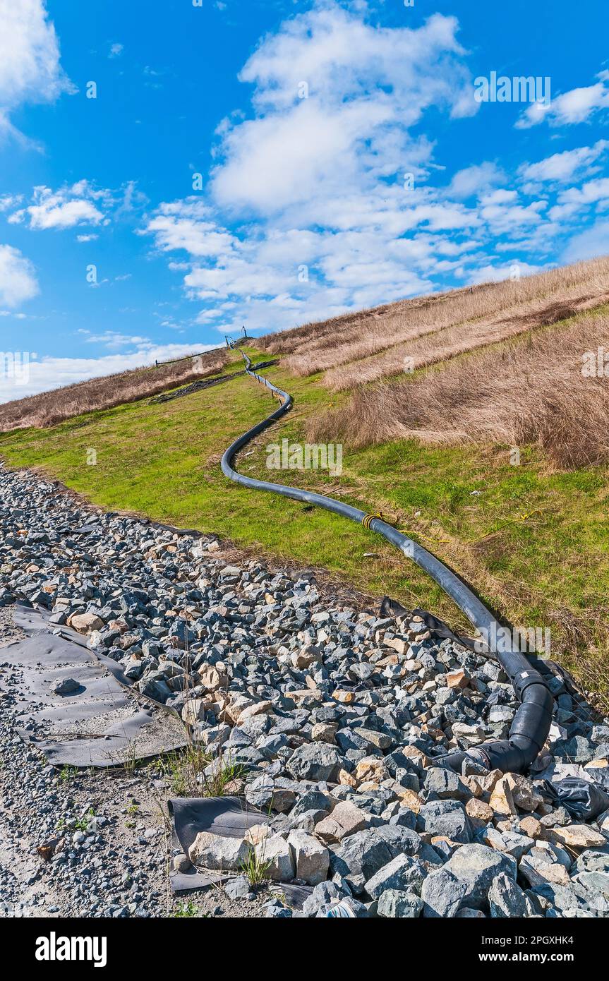 A hillside with growth and brush, with a rock layer for drainage, and a ...