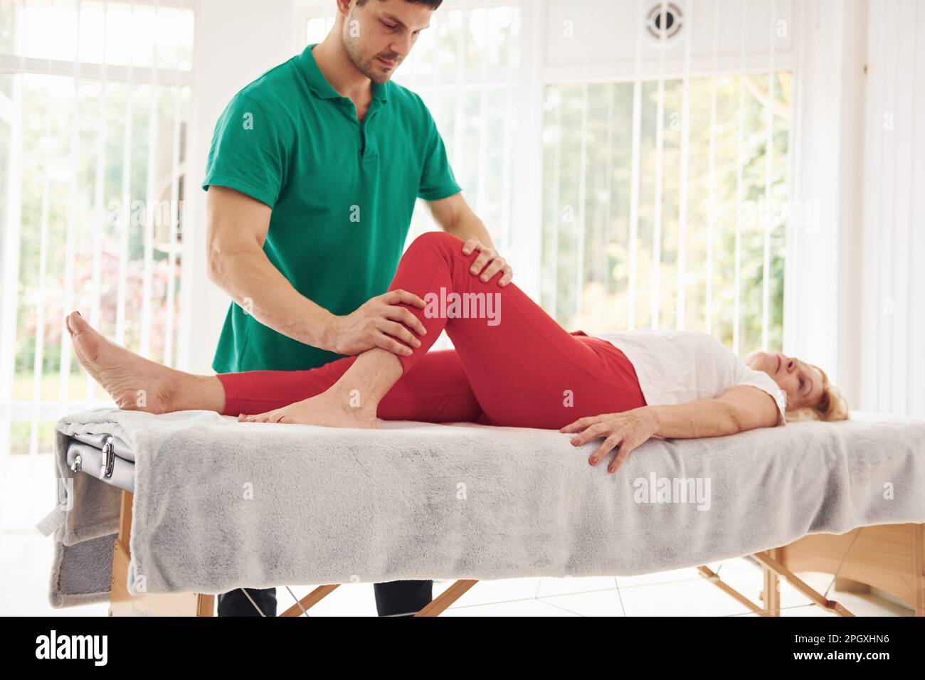 Older woman have a visit in clinic, lying down and having rehabilitation. Male instructor ...