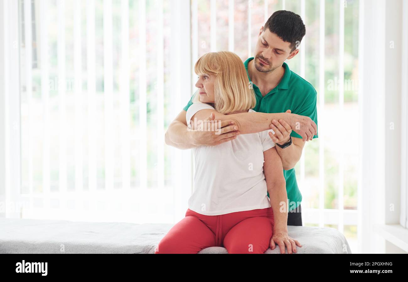 Older woman have a visit in clinic and having rehabilitation. Male instructor helping her Stock ...