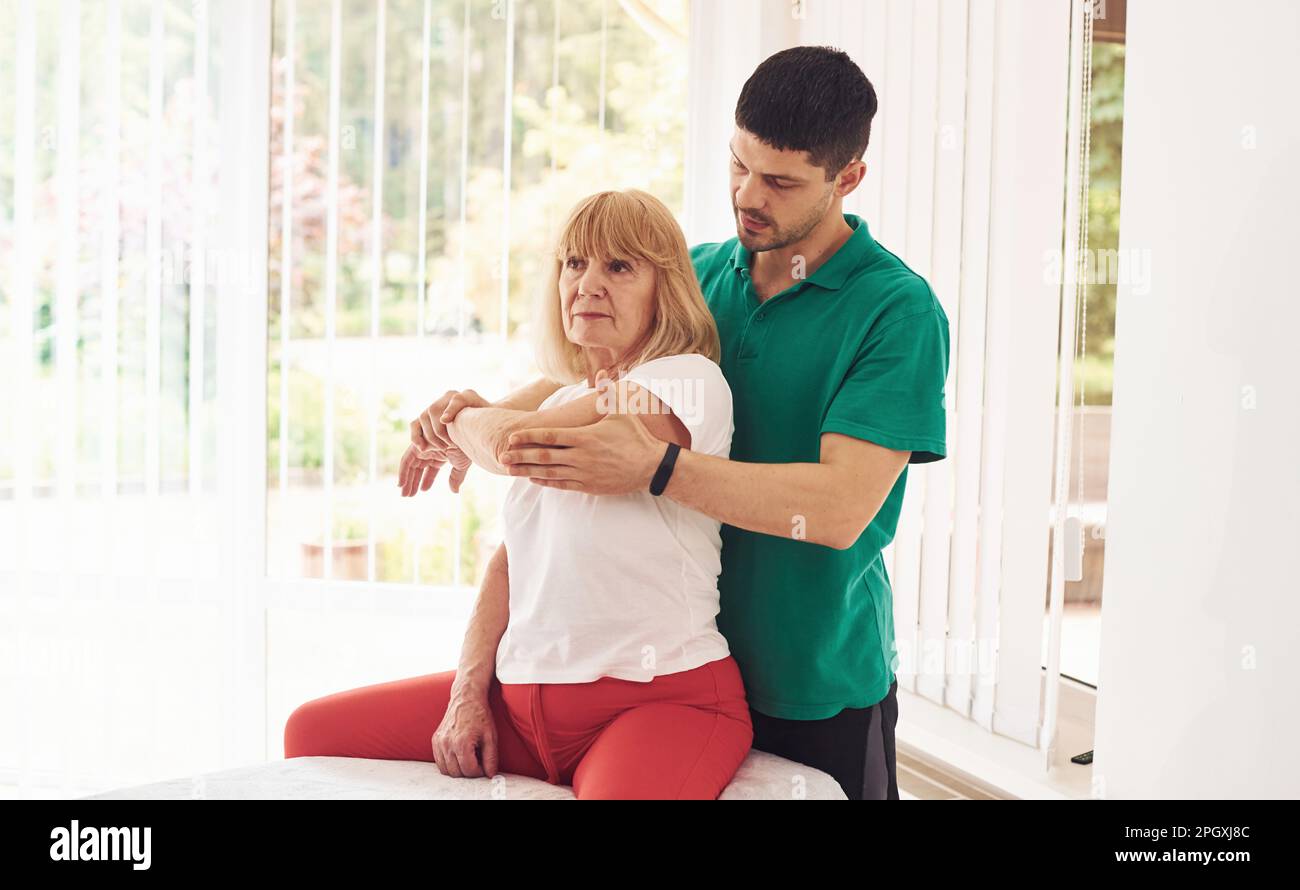 Older woman have a visit in clinic and having rehabilitation. Male instructor helping her Stock ...