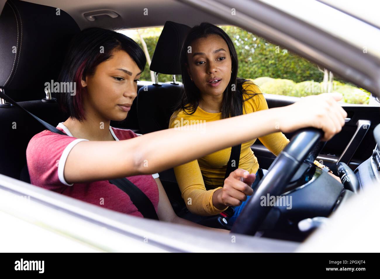 Happy biracial sisters sitting in car talking, one sister giving the ...