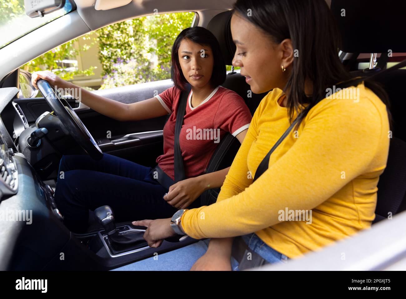 Happy biracial sisters sitting in car talking, one sister giving the ...
