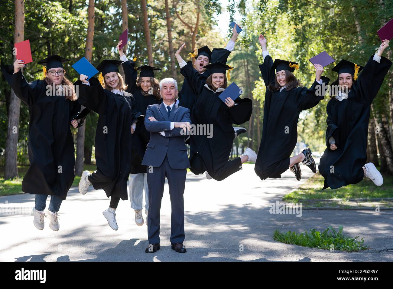 A university professor and seven robed graduates are jumping outdoors ...