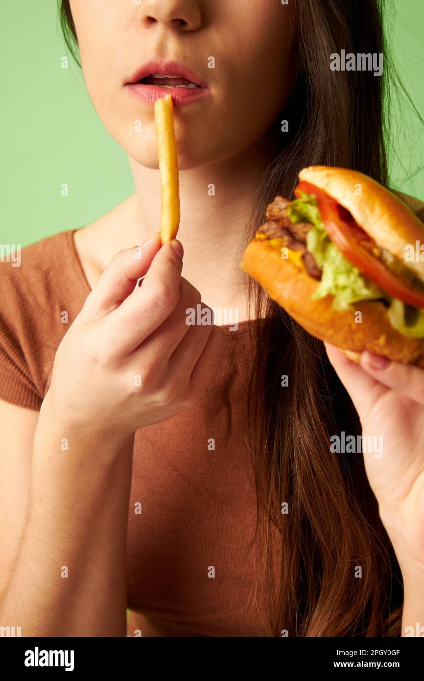Portrait of woman holding a hamburger cheeseburger while eating french ...