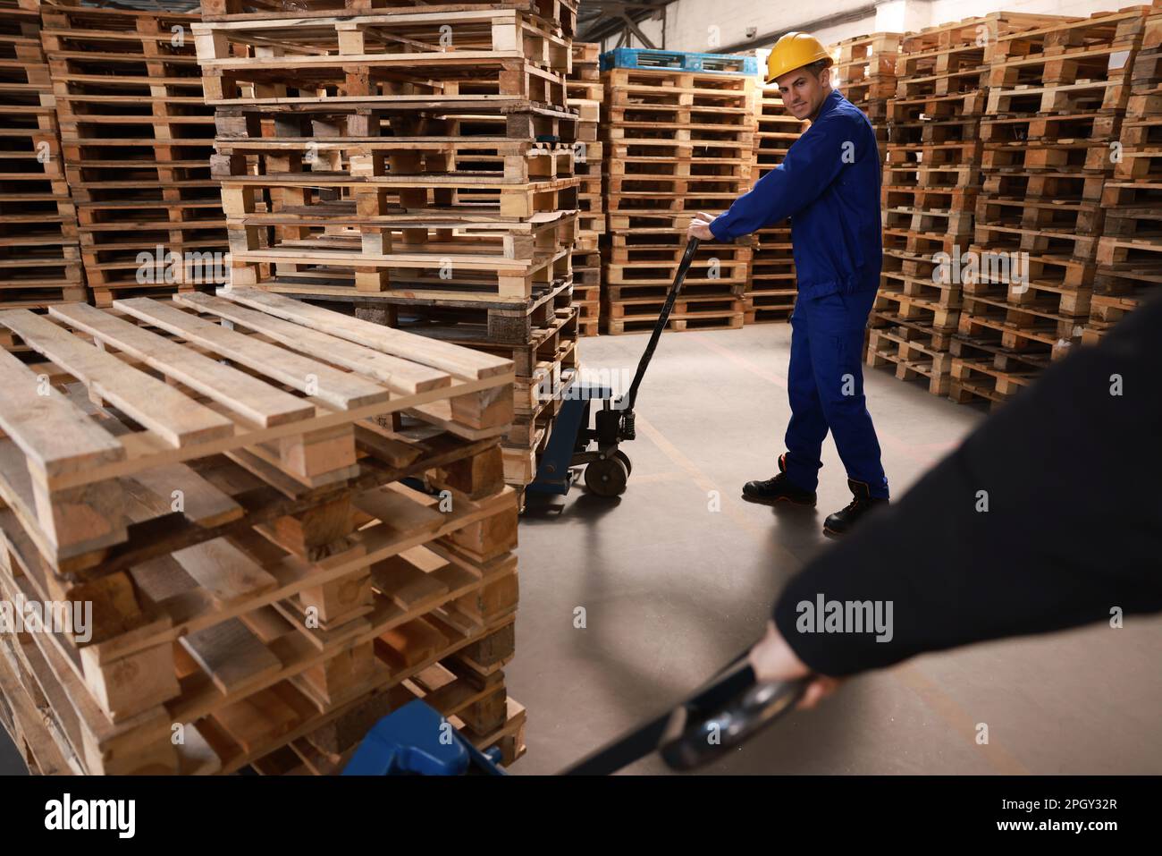 Workers moving wooden pallets with manual forklift in warehouse Stock ...