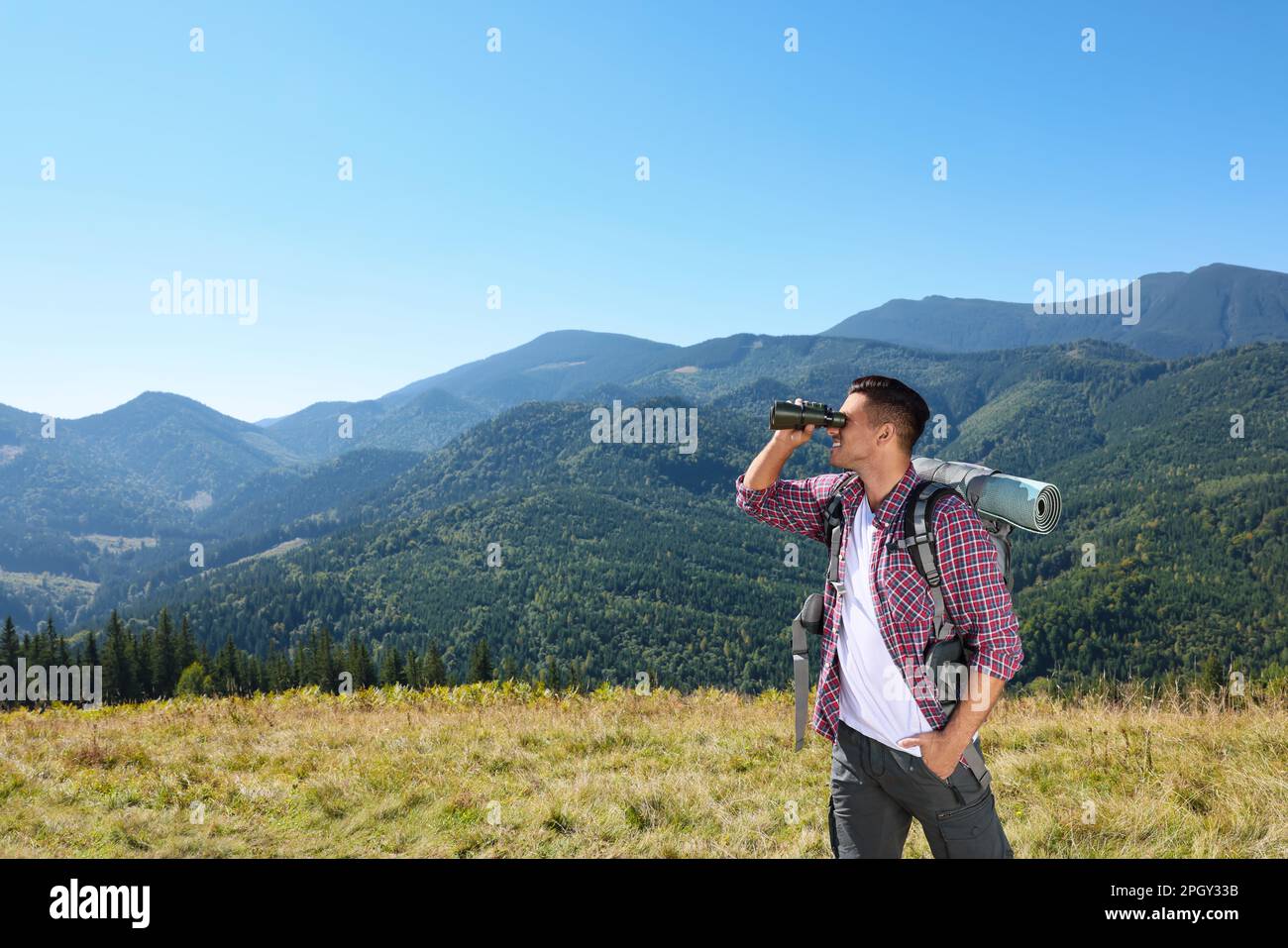 Tourist with hiking equipment looking through binoculars in mountains ...