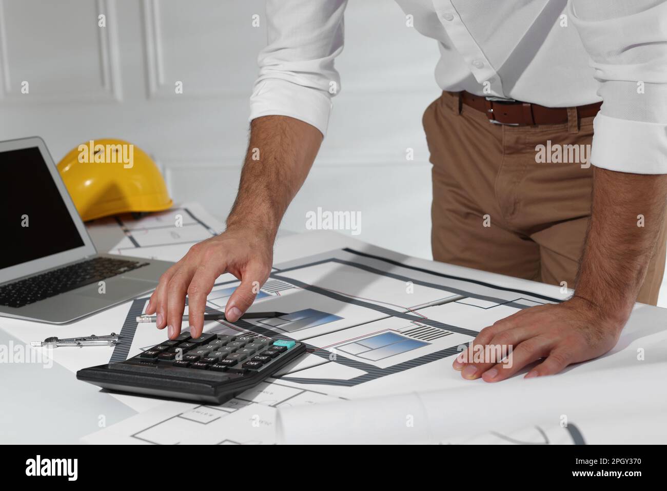 Architect working with construction drawings and calculator indoors ...