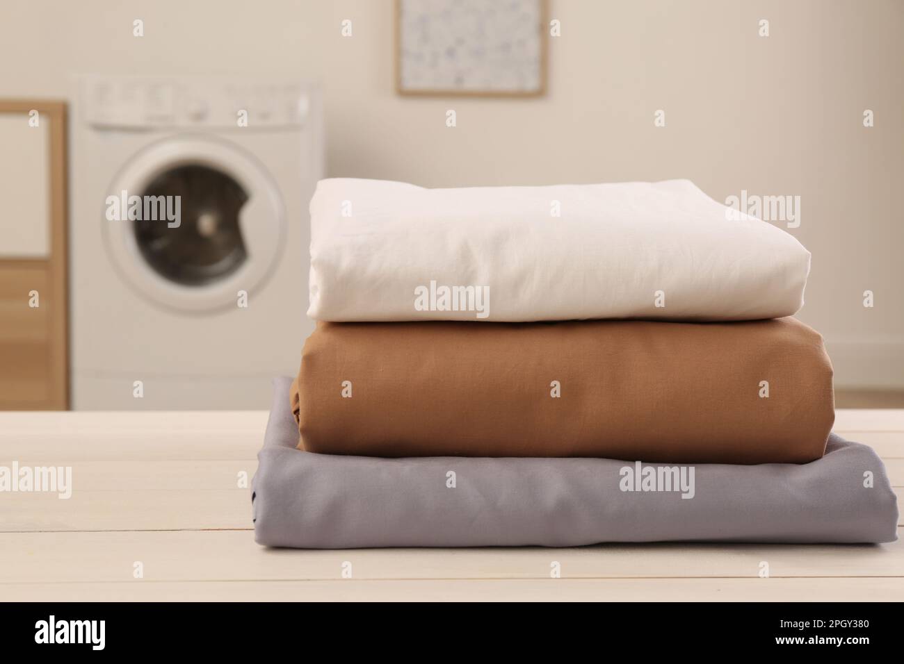 Stack of clean bed linens on white wooden table in laundry room Stock ...