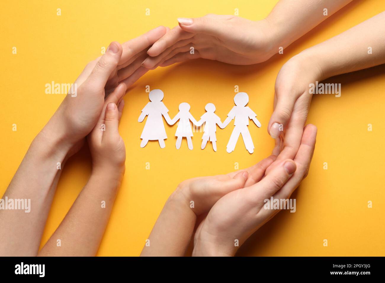 Parents and child protecting paper cutout of family on orange ...