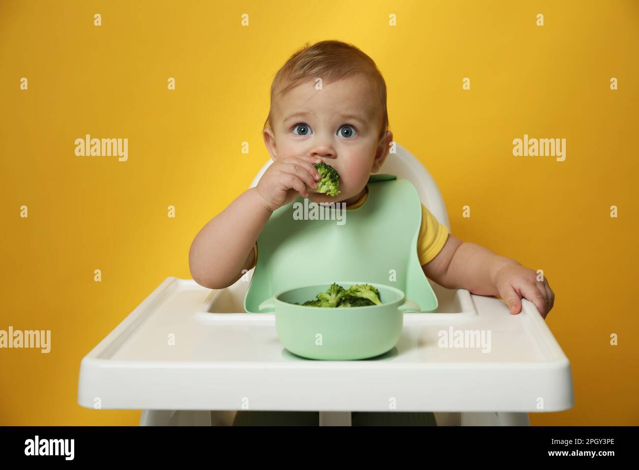 Cute little baby wearing bib while eating on yellow background Stock ...