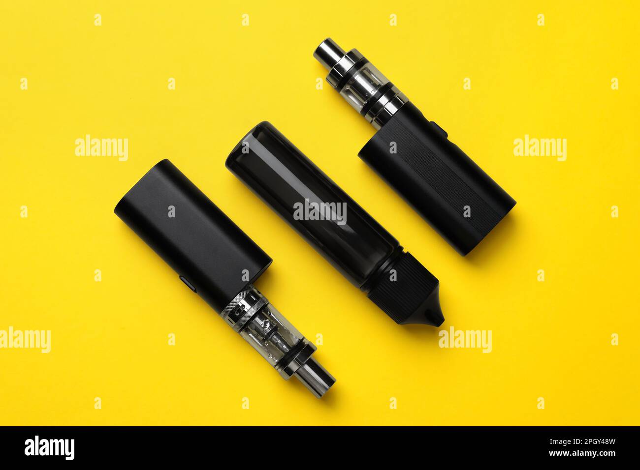 Electronic cigarettes and vaping liquid on yellow background, flat lay ...