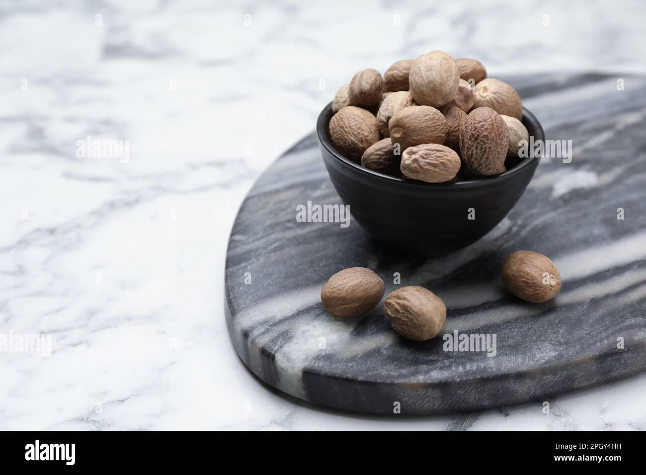 Bowl with nutmeg seeds on white marble table. Space for text Stock ...