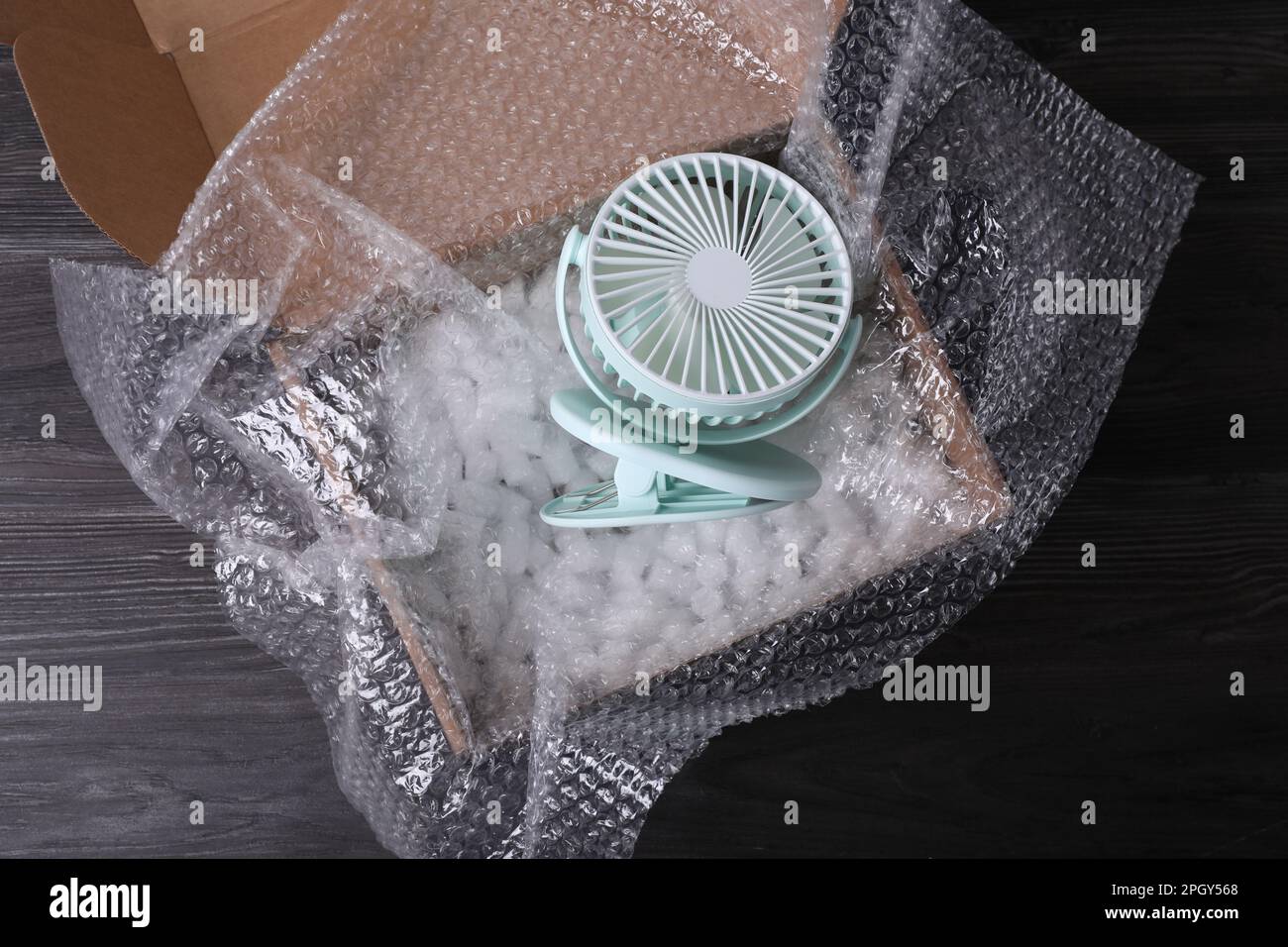 Small fan with bubble wrap and packaging foam in cardboard box on dark ...