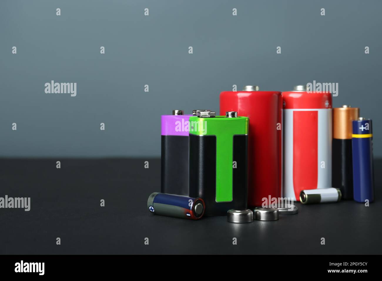 Different types of batteries on black table against grey background ...
