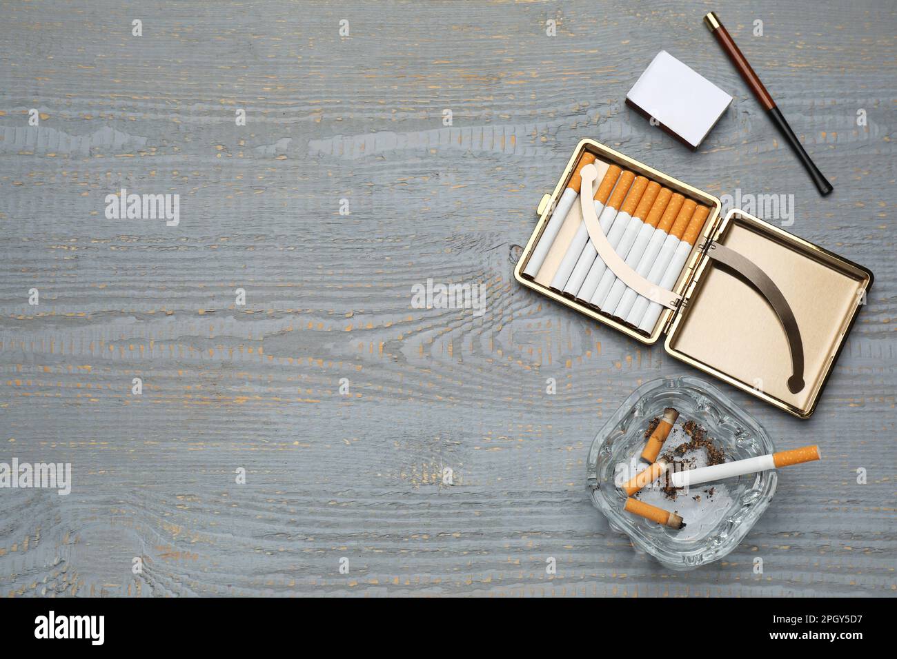 Cigarettes in case, holder, matchbox and ashtray with stubs on grey ...