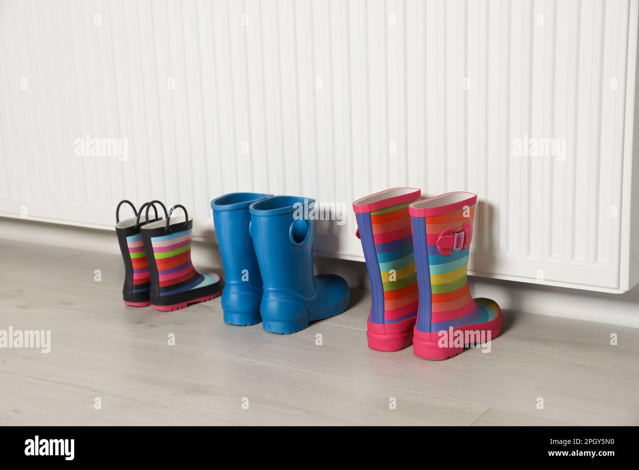 Different pairs of boots near modern radiator indoors Stock Photo - Alamy