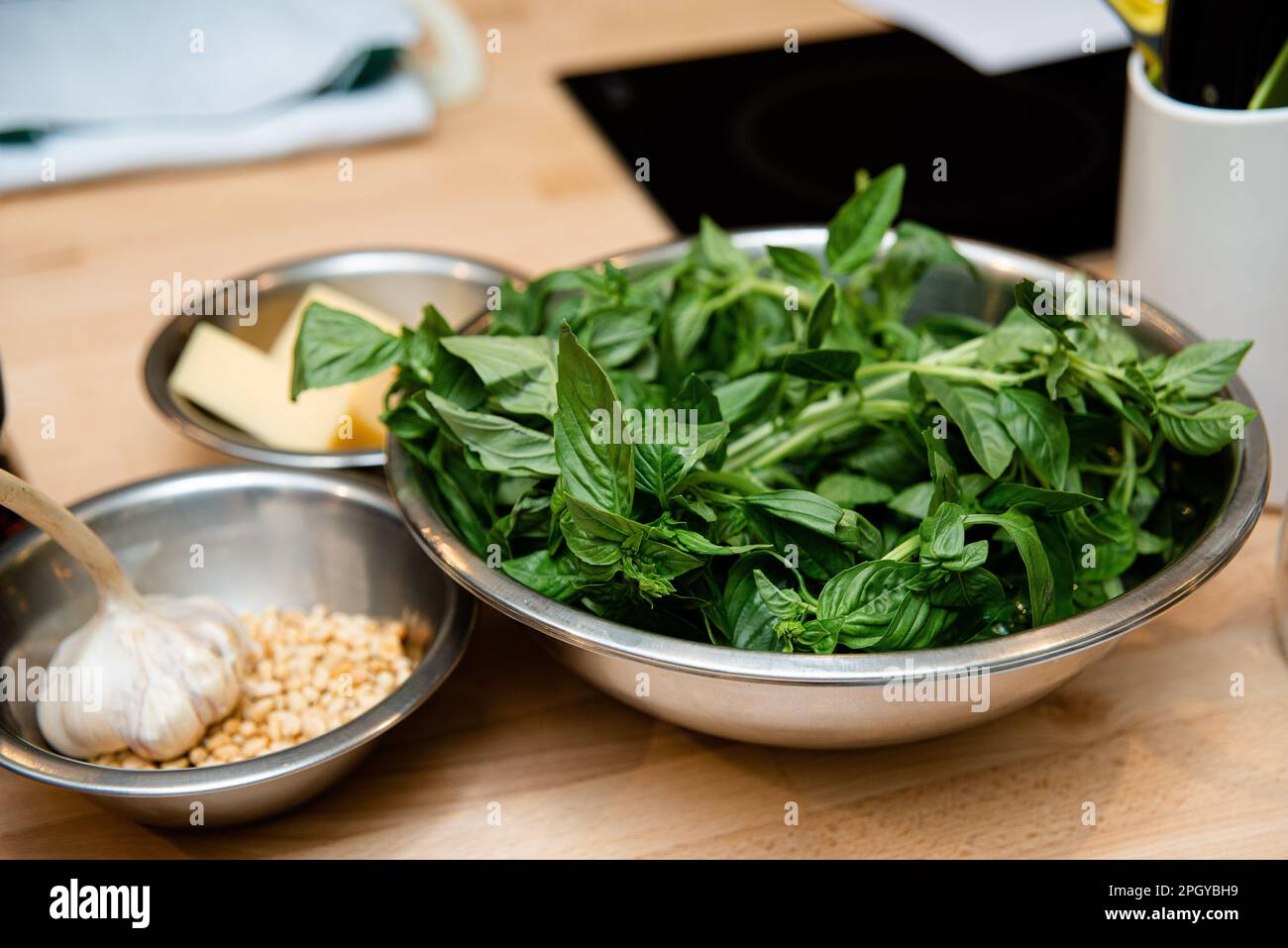 Fresh basil leaves, garlic and pine nuts, parmesan cheese in metal bowls on wooden table. Raw ...