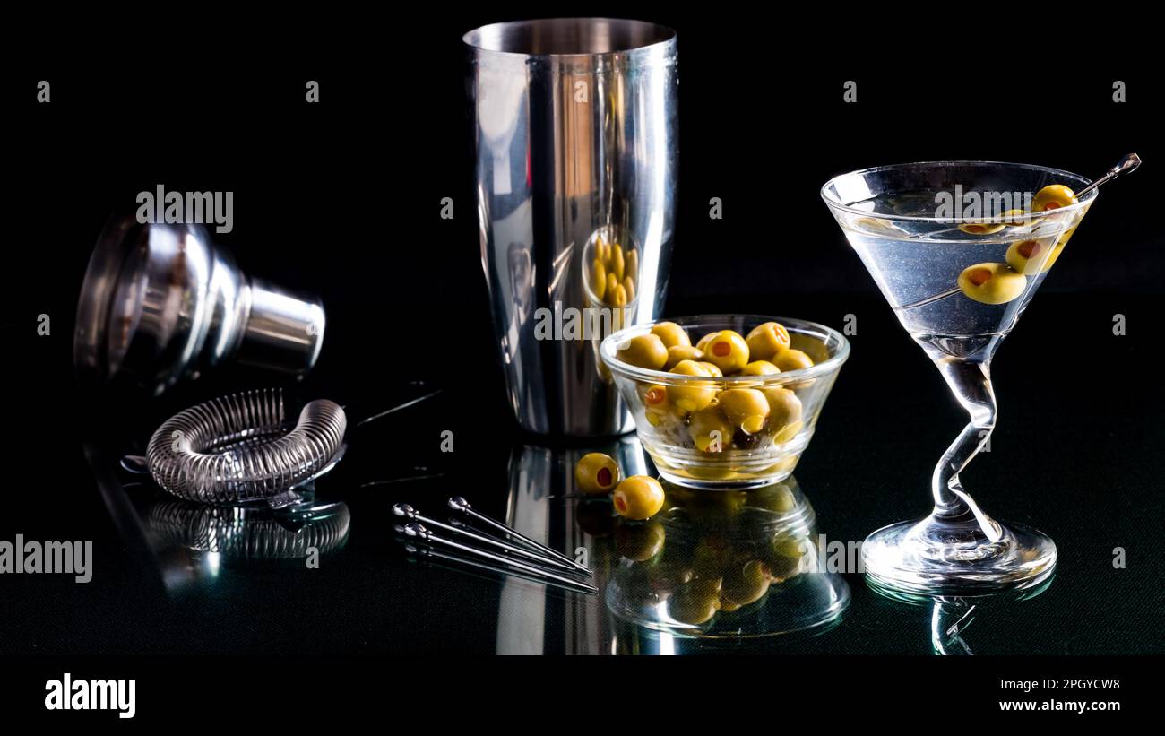 A classic Martini with a pick of green olives, against a black ...