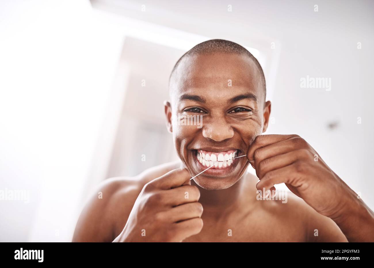 Your smile says a lot about you. a handsome young man flossing his teeth in the bathroom at home ...