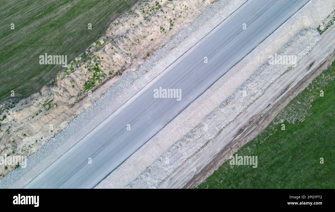 Asphalt road under construction between two green fields. View from the ...