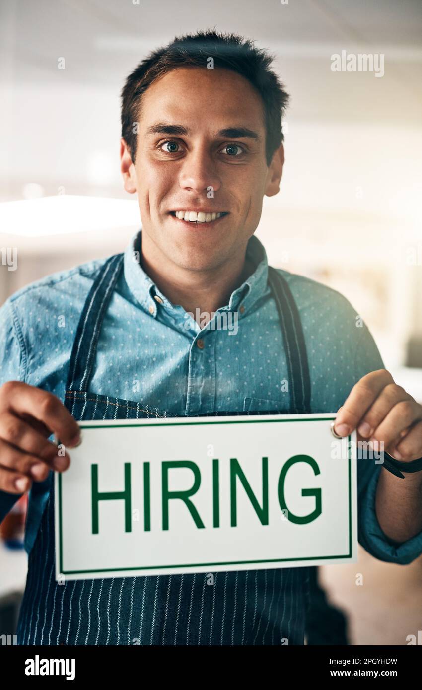 Staff wanted. a young man holding up a hiring sign in his store Stock ...