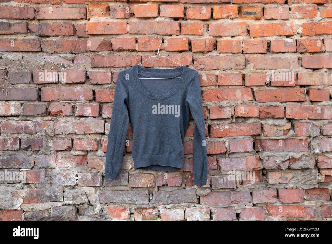 dark blue jacket hanging on a hanger on an old brick wall in the street ...